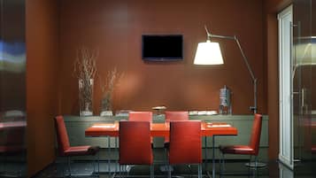 Uma sala de conferências moderna com uma mesa comprida, quatro cadeiras, uma TV de tela plana e uma luminária pendente.