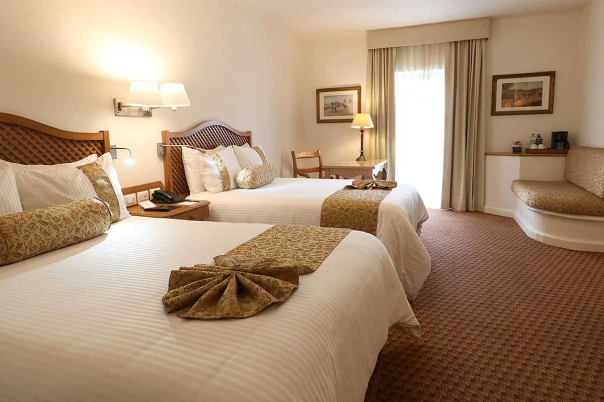 Quarto de hotel com duas camas, uma escrivaninha, uma cadeira e um sofá.