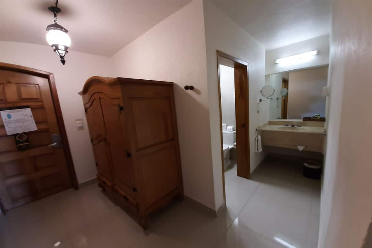 Corredor com guarda-roupa de madeira, porta para um banheiro com espelho e pia.