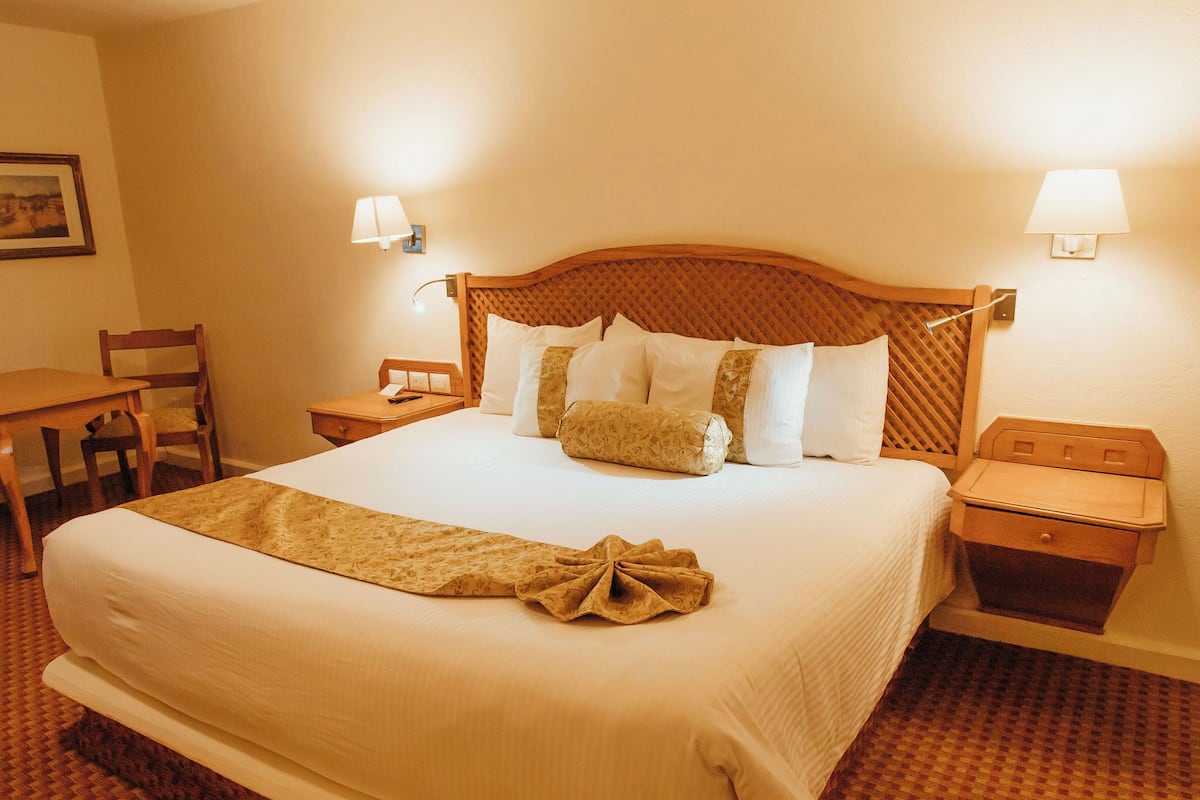 Quarto de hotel com uma cama grande, duas mesas de cabeceira, uma cadeira e um abajur em cada parede.