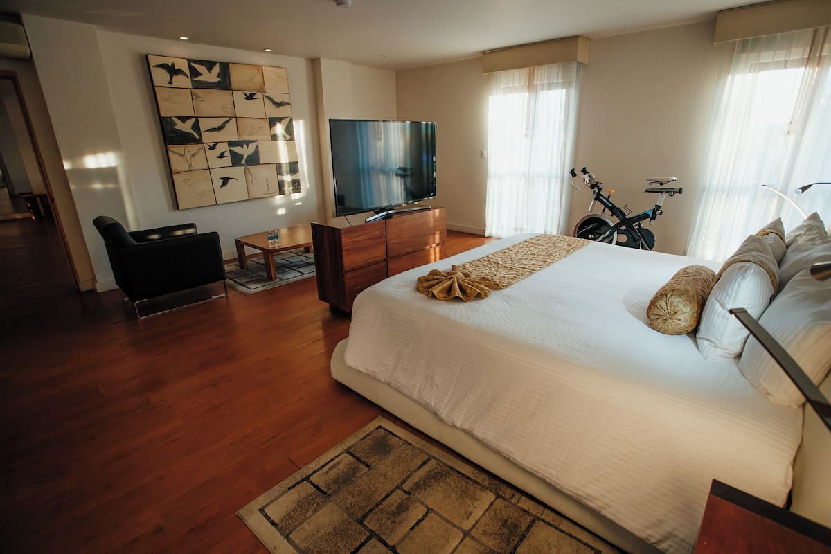 Quarto de hotel com uma cama grande, televisão, escrivaninha e uma bicicleta.