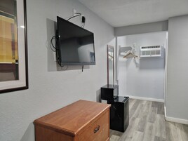 Quarto com televisão de tela plana na parede, cômoda de madeira, geladeira preta e espelho.
