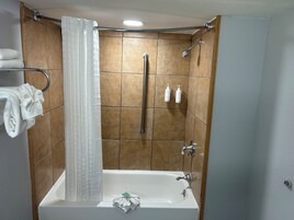 Uma casa de banho com banheira, chuveiro com barra de apoio e toalheiro com toalhas.