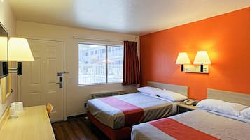 Quarto de hotel com duas camas, janela com vista para edifícios, uma porta e mesa com abajur.