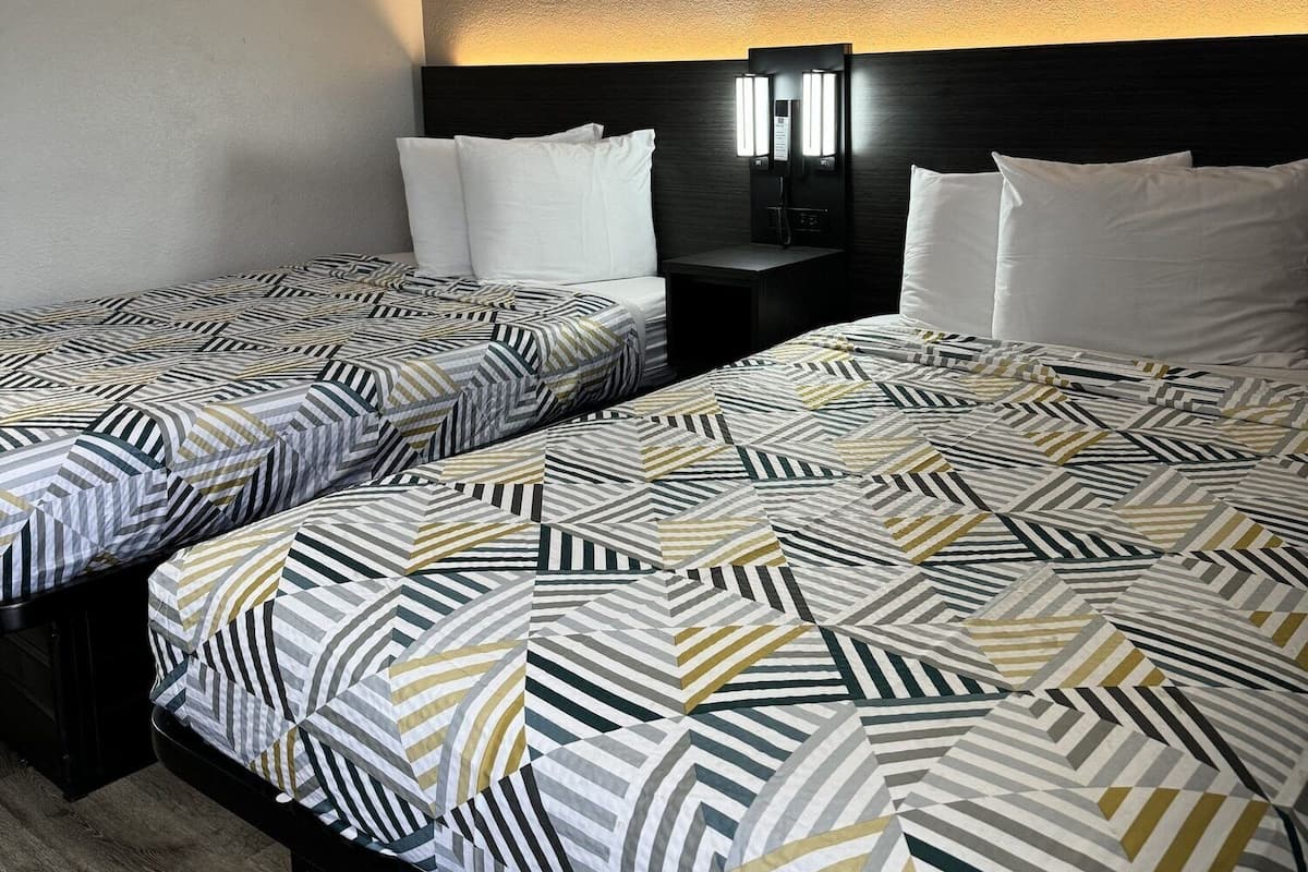 Quarto de hotel com duas camas, cada uma com roupa de cama estampada, mesa de cabeceira com abajur e cabeceira com luminária.