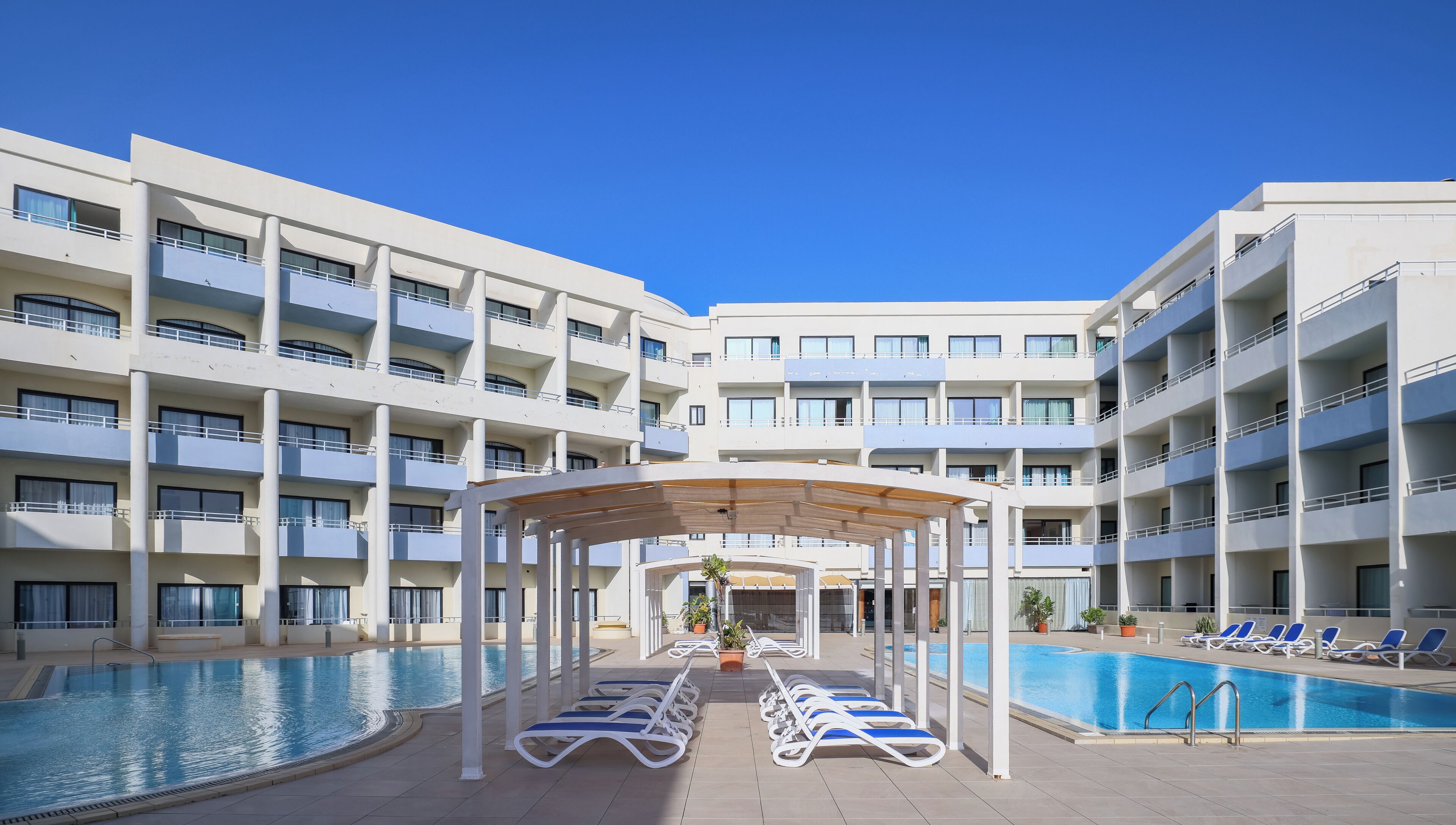 Hotel com piscina, várias varandas e área de estar coberta.