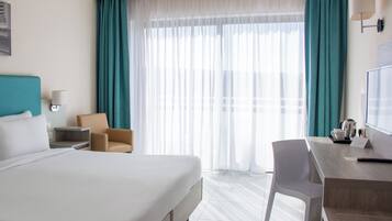 Quarto de hotel com uma cama grande, uma escrivaninha com cadeira, televisão e janela com cortinas.