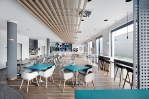 Uma cafeteria moderna com mesas compridas, cadeiras e teto alto com ripas de madeira.