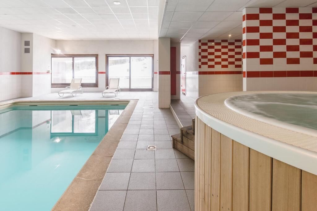 Piscina interna com hidromassagem, piso revestido e padrão de parede xadrez.