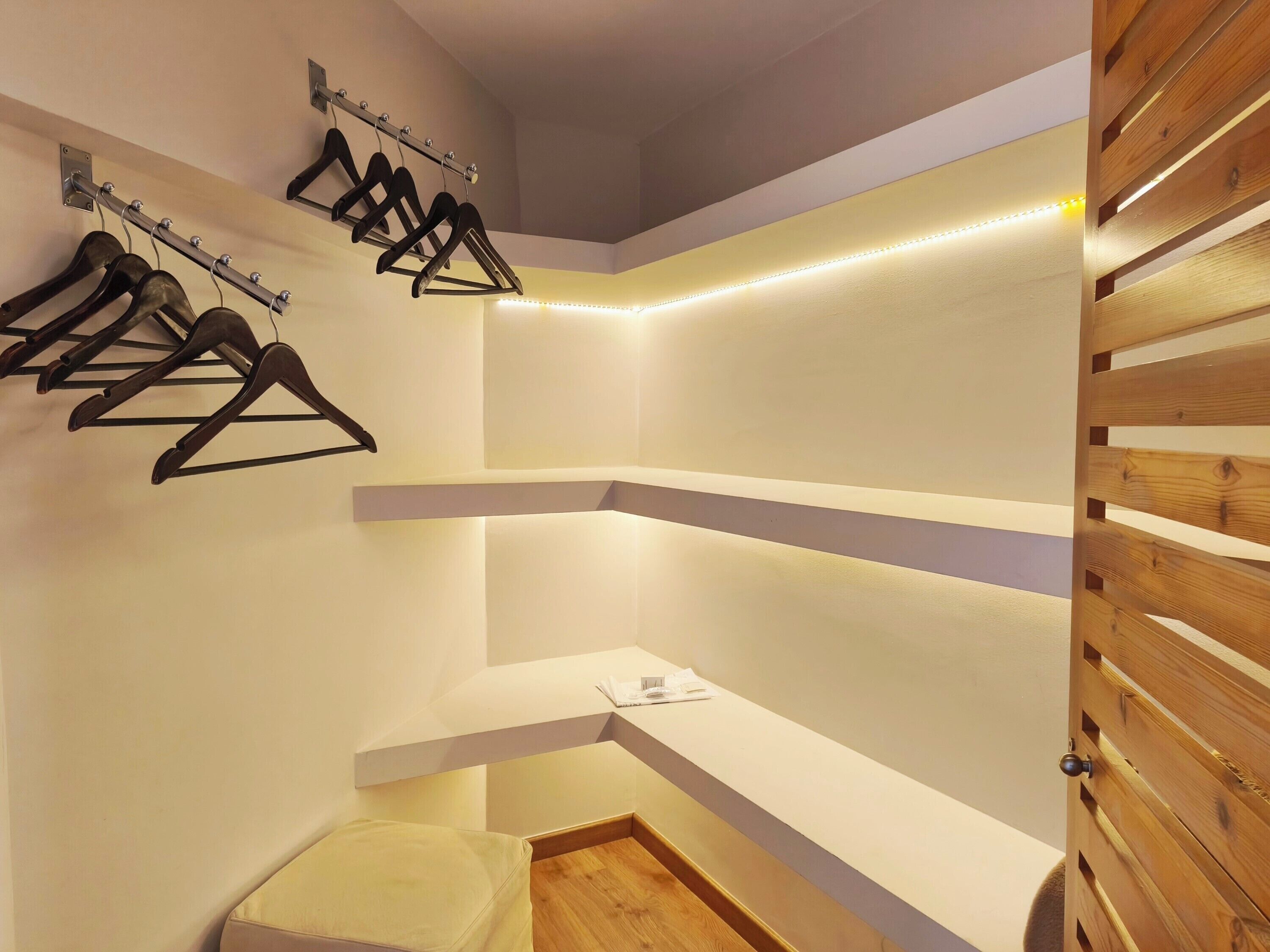 Um banheiro moderno com um banco de madeira, um porta-toalhas com vários cabides e uma porta de madeira.