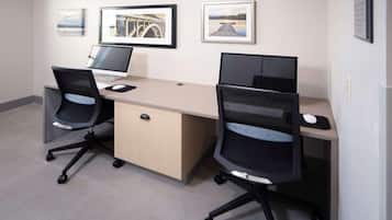 Um espaço de escritório moderno com duas mesas, cada uma com um computador e uma cadeira. Há quadros nas paredes.