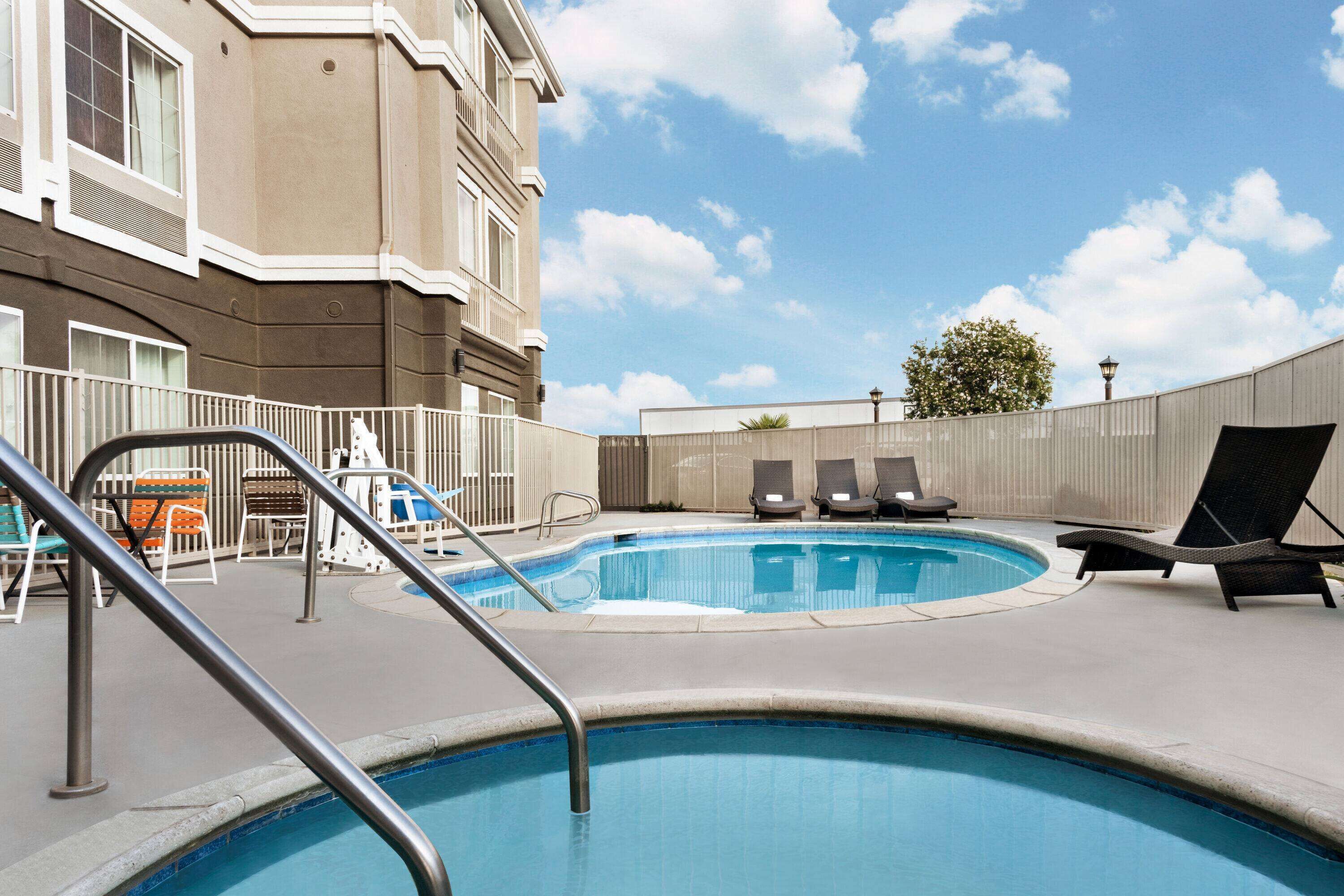 Piscina com espreguiçadeiras e um edifício ao fundo.