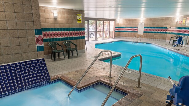 Piscina interior com chão revestido de azulejos, escada de piscina e algumas cadeiras.
