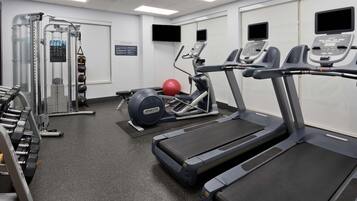 Centro de ginástica com esteiras, um banco de musculação e uma máquina de polia.
