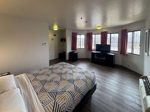 Um quarto de hotel espaçoso com uma cama grande, uma escrivaninha com computador, televisão e uma janela com cortinas.