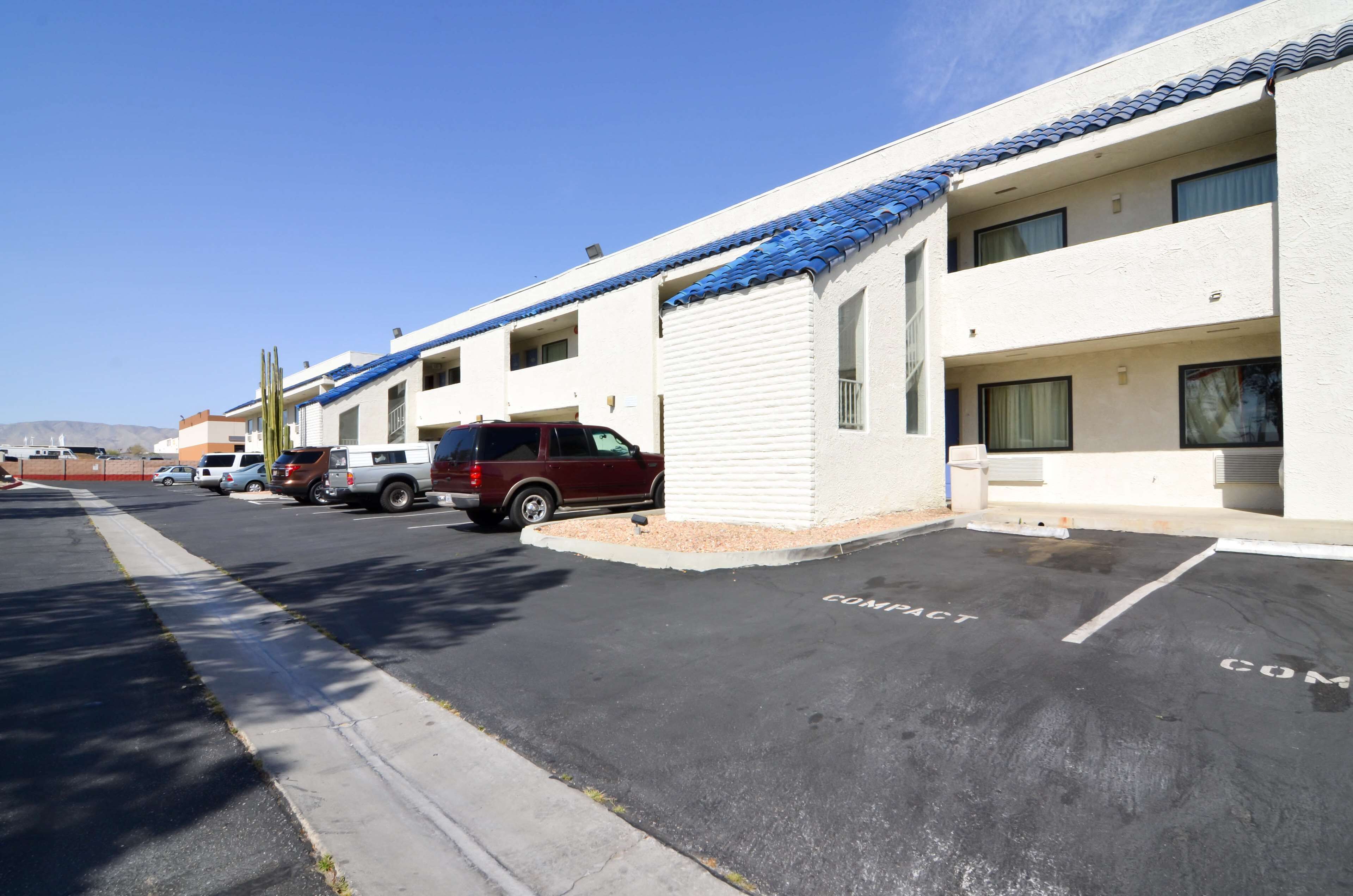 Fileira de edifícios de motel térreos, com telhados azulejados em azul e um estacionamento na frente.