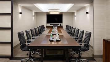 Uma sala de conferência com uma mesa comprida, cadeiras pretas e uma tela de projetor.
