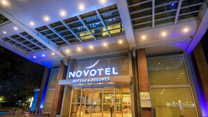 Entrada de um hotel Novotel com design moderno, grandes janelas de vidro e fachada bem iluminada.