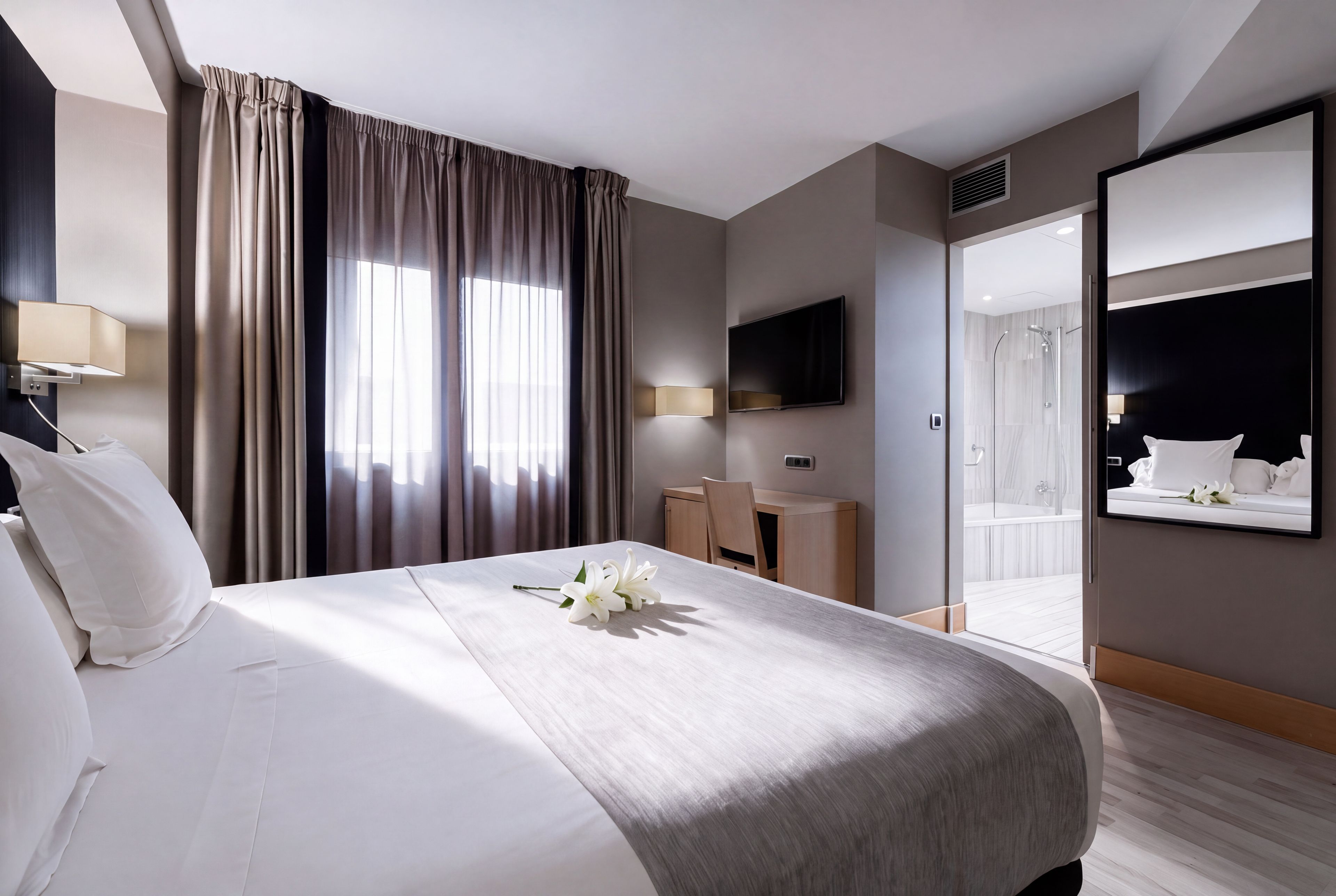 Quarto de hotel com uma cama grande, uma escrivaninha, uma televisão e um banheiro visível através de uma porta aberta.