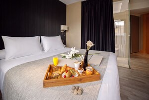Quarto de hotel com cama, bandeja de itens de café da manhã, vaso com flores e vista para o banheiro.