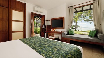 Quarto de hotel com cama, escrivaninha, televisão e vista para o mar.