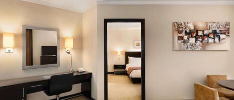 Quarto de hotel com escrivaninha, cadeira, cama e área de refeições com cadeiras.