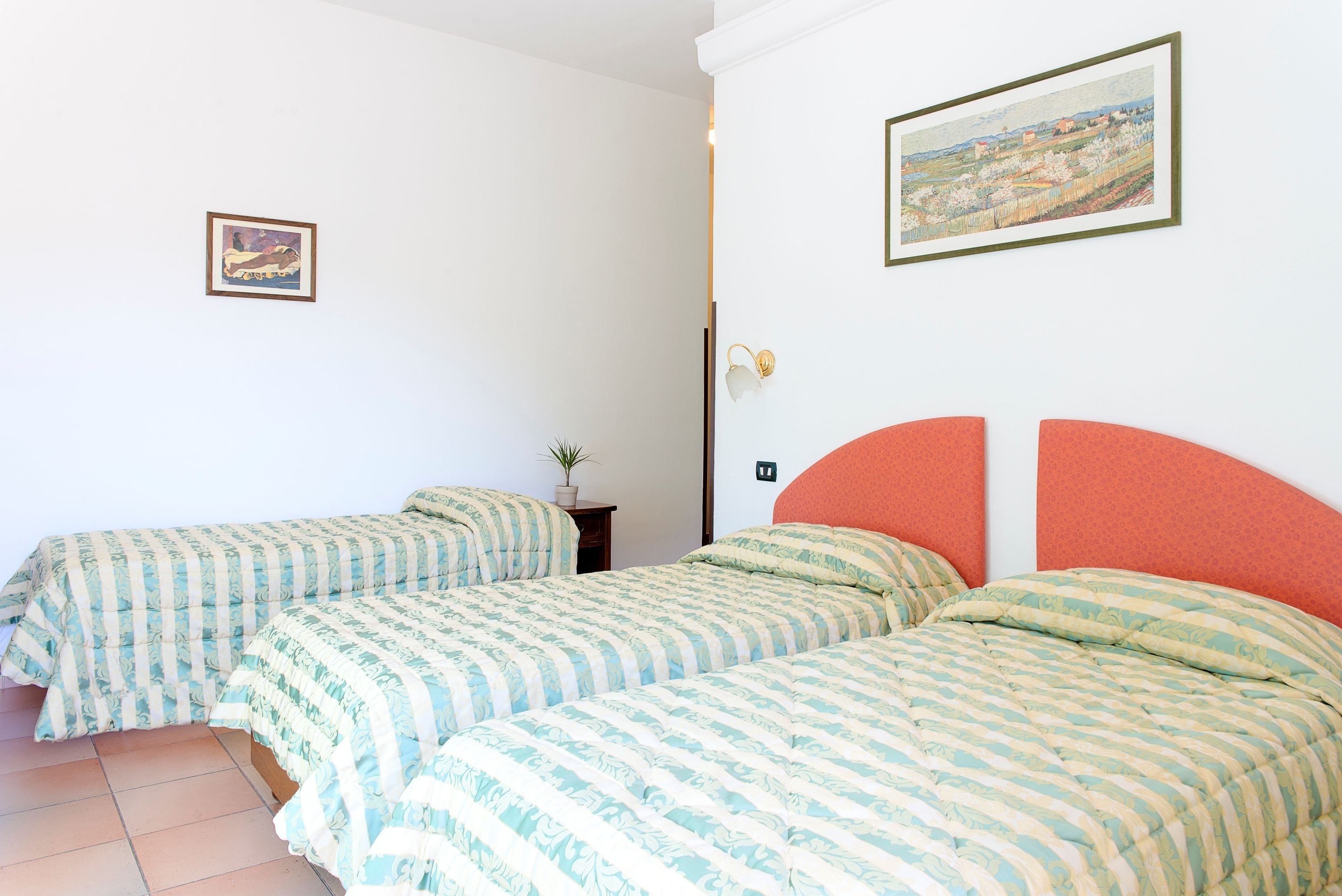 Quarto com duas camas, uma pequena mesa de cabeceira com uma planta e um quadro na parede.