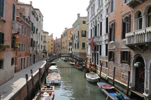 Um canal estreito em Veneza, com barcos atracados nas margens e uma ponte ao longe.