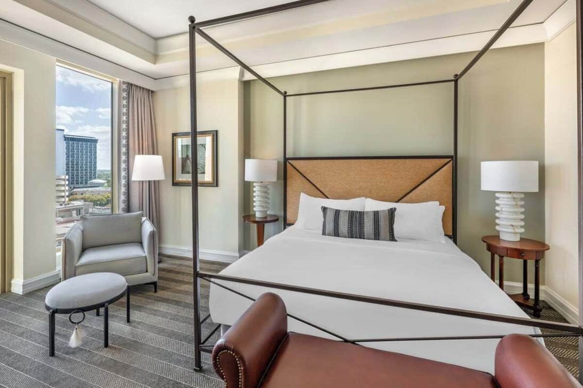 Uma cama de dossel com vista para a cidade, uma cadeira, um abajur e uma mesinha.
