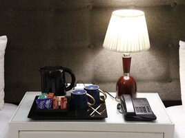 Quarto de hotel com mesa de cabeceira que inclui cafeteira, duas chávenas, telefone e um tabuleiro com petiscos.