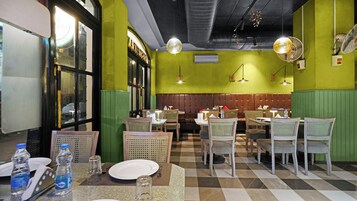 Interior de restaurante com paredes verdes, chão quadriculado e diversos tipos de assentos, incluindo cabines e mesas.