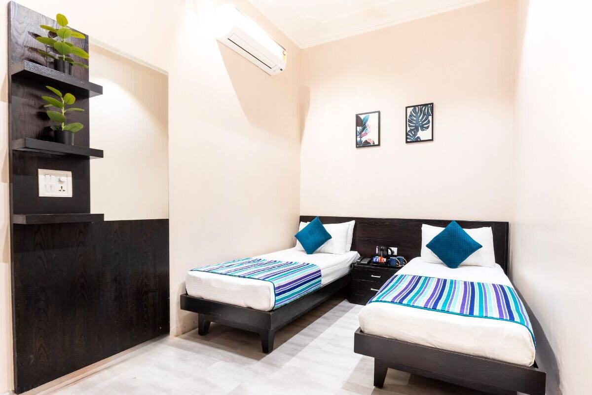 Quarto com duas camas, uma mesinha de cabeceira, prateleira na parede com plantas e um aparelho de ar condicionado.
