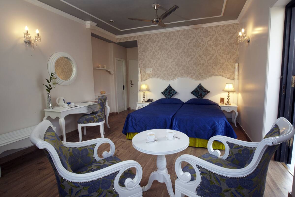 Quarto de hotel com uma cama, duas mesas de cabeceira, uma escrivaninha, uma cadeira e uma mesinha redonda.