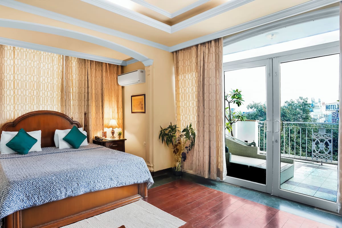Quarto espaçoso com uma cama grande, mesa de cabeceira, abajur e vista para o exterior.