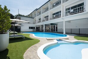 Um edifício moderno com piscina, área de estar externa e um gramado bem cuidado.