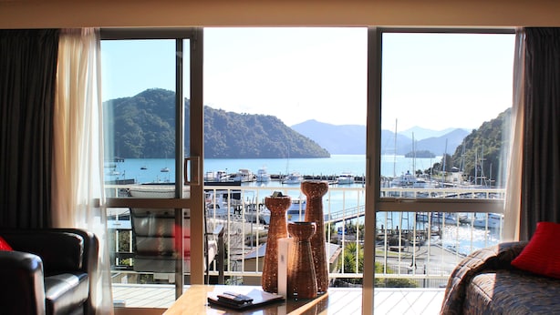 Quarto de hotel com uma grande janela que oferece vista para uma marina e montanhas.