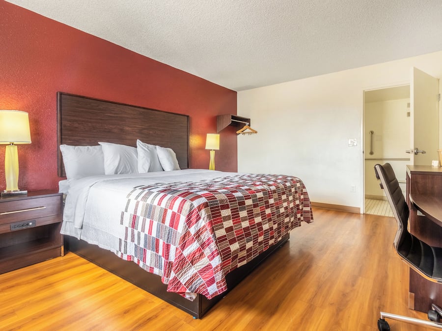 Quarto de hotel com cama, mesas de cabeceira, escrivaninha e uma cadeira.