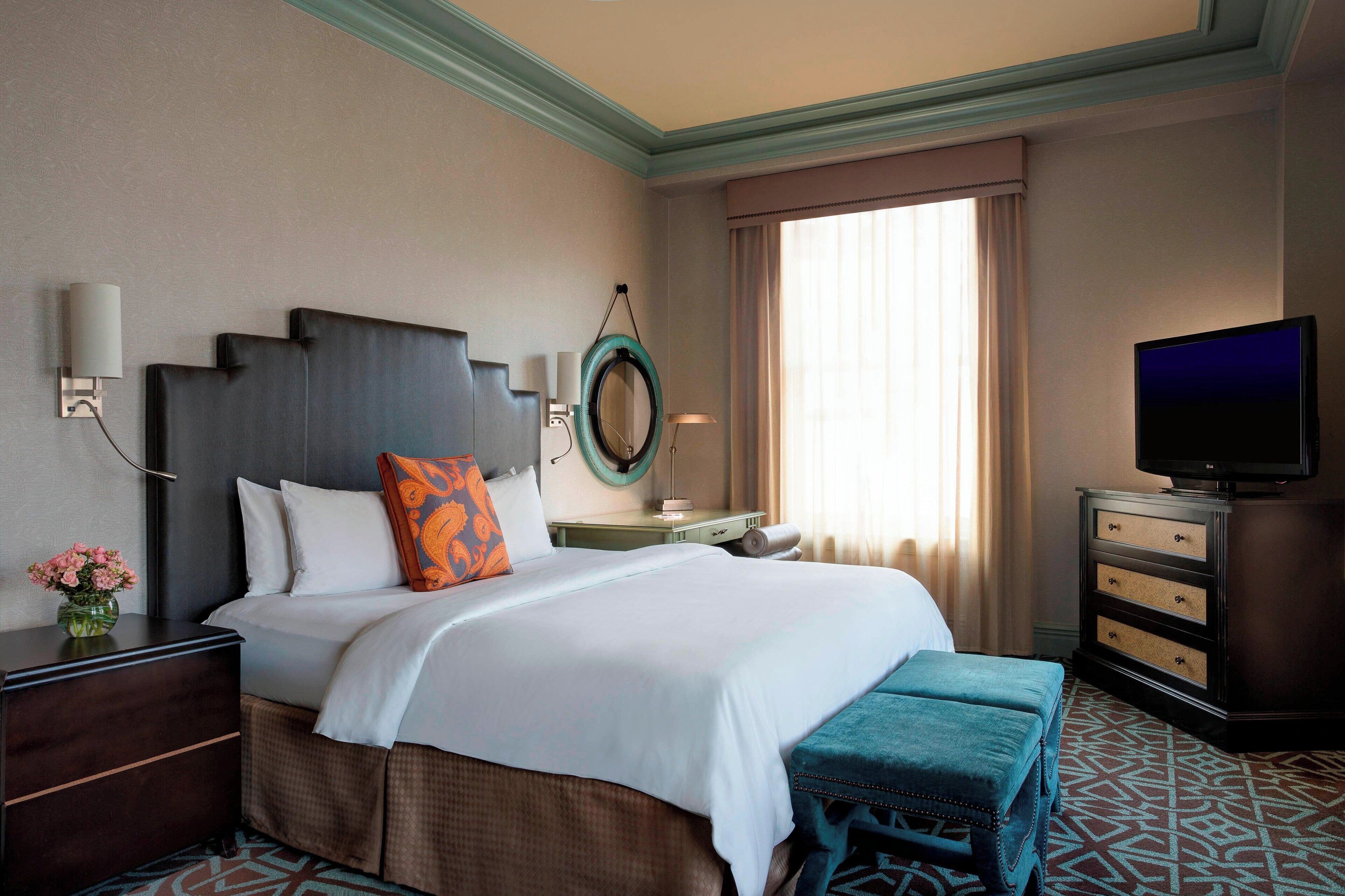 Quarto de hotel com uma cama grande, televisão, escrivaninha e janela com cortinas.