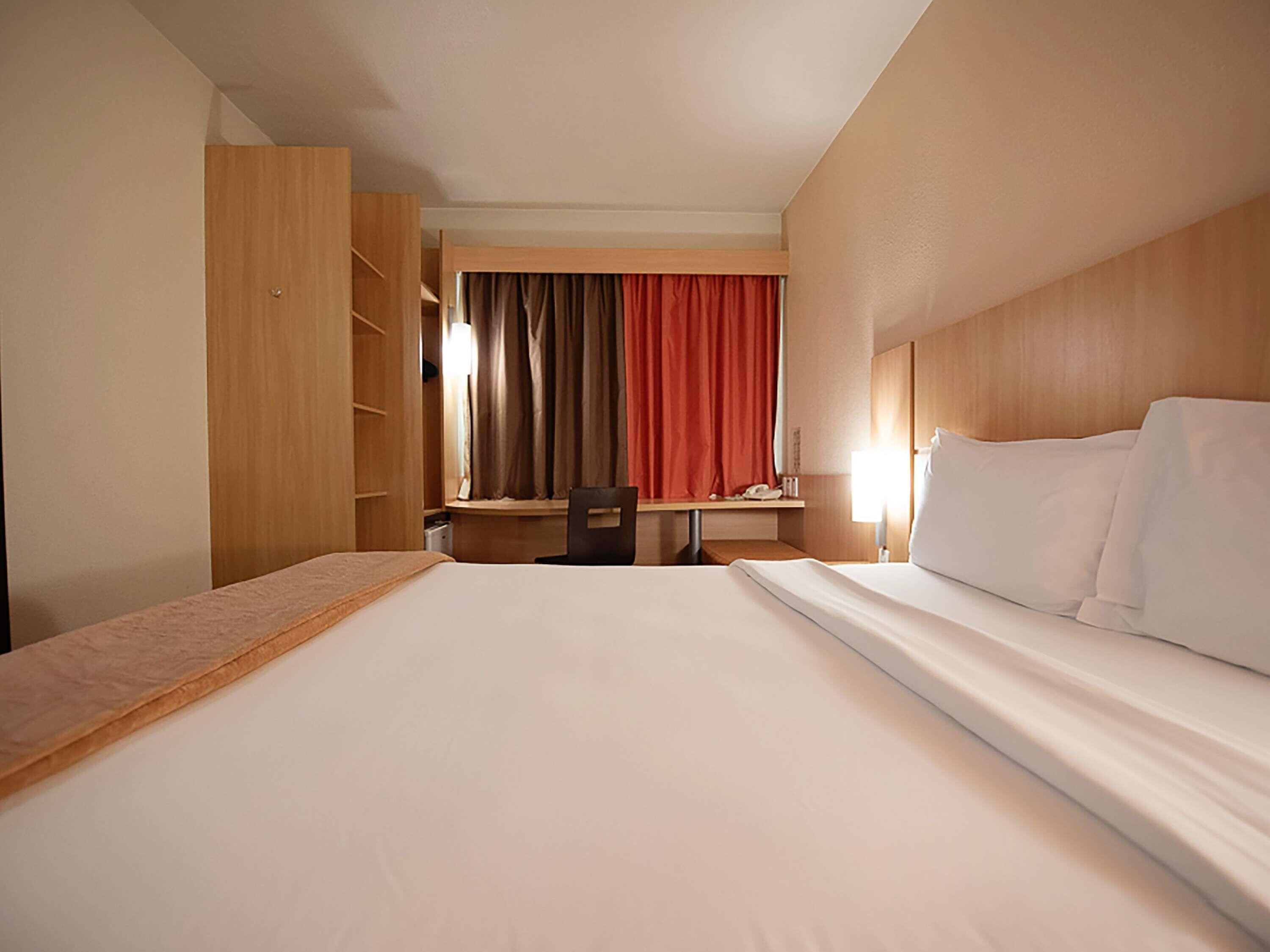 Quarto de hotel com cama, escrivaninha, cadeira e guarda-roupa.