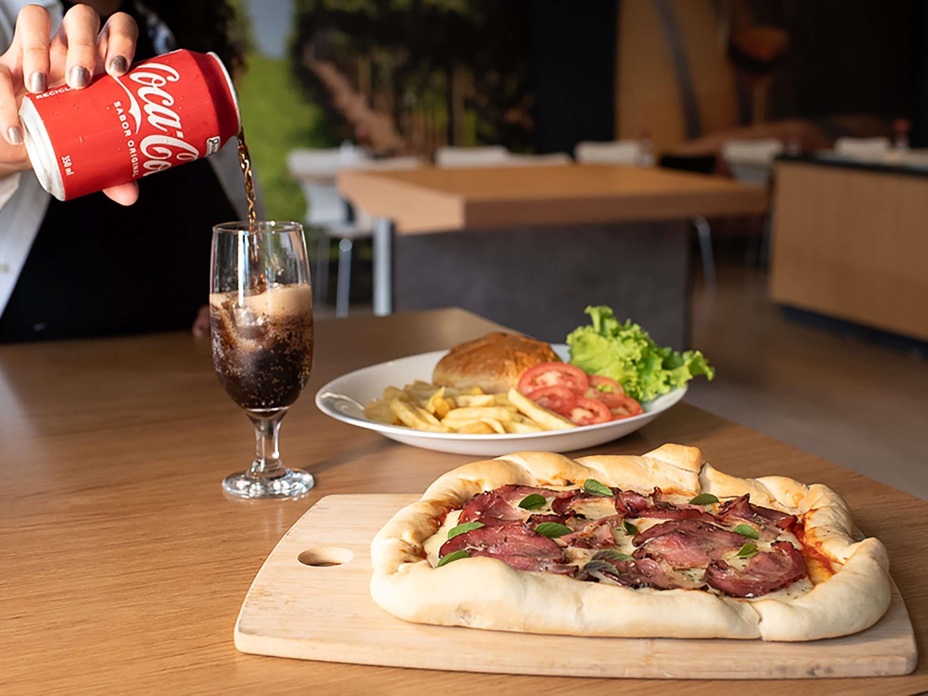 Uma refeição com sanduíche, batatas fritas e pizza sobre uma mesa de madeira.