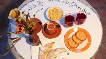 Uma mesa com um prato de croissants, uma tigela de cereais e dois copos de bebida vermelha.