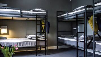 Um quarto em dormitório com beliches, uma mesa de cabeceira e uma luminária.