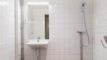 Uma casa de banho moderna com lavatório branco, espelho e chuveiro.