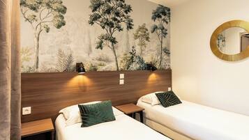 Quarto de hotel com duas camas de solteiro, uma mesa de cabeceira, uma luminária na parede e uma grande pintura de árvores.