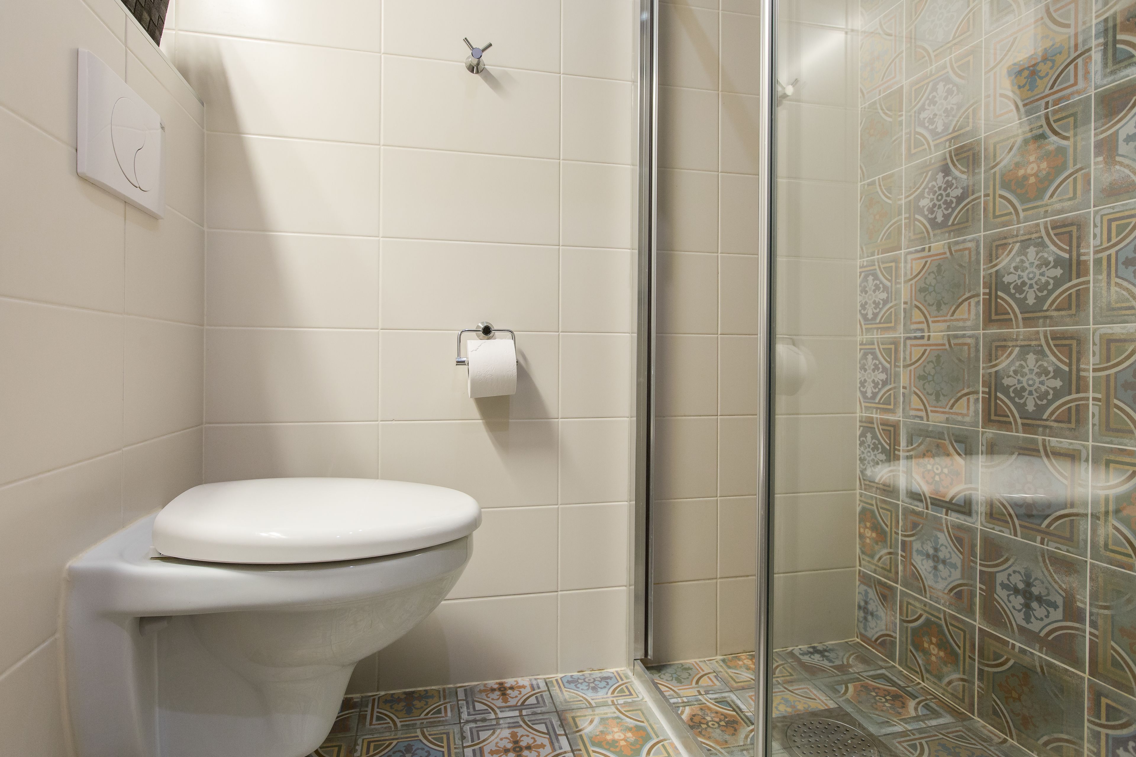 Um banheiro com vaso sanitário, chuveiro com porta de vidro e azulejos estampados nas paredes e no chão.