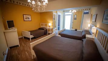 Quarto de hotel com duas camas, uma escrivaninha, uma cadeira, uma TV e um candelabro.