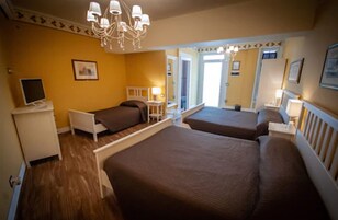 Quarto de hotel com duas camas, uma escrivaninha, uma cadeira, uma TV e um candelabro.