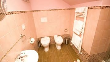 Um banheiro com paredes cor-de-rosa, pia, dois vasos sanitários, porta-toalhas e área de chuveiro.