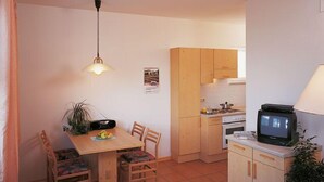 Uma cozinha compacta com armários de madeira, uma mesa de jantar com cadeiras, uma televisão e um lustre.