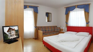 Quarto de hotel com uma cama grande, um sofá, uma televisão e uma janela com cortinas.